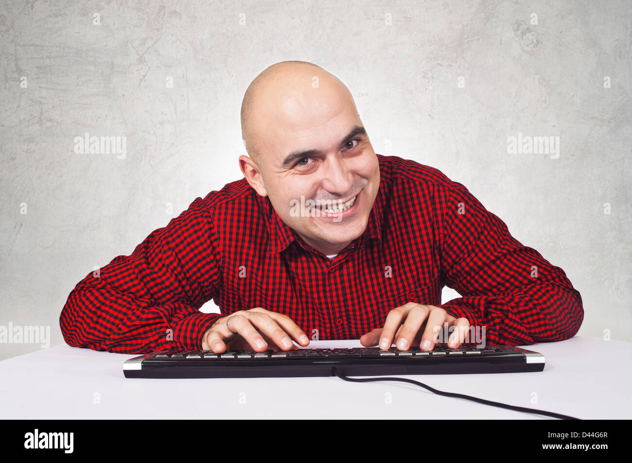Bald young adult man sitting at the table with keyboard in front of the ...
