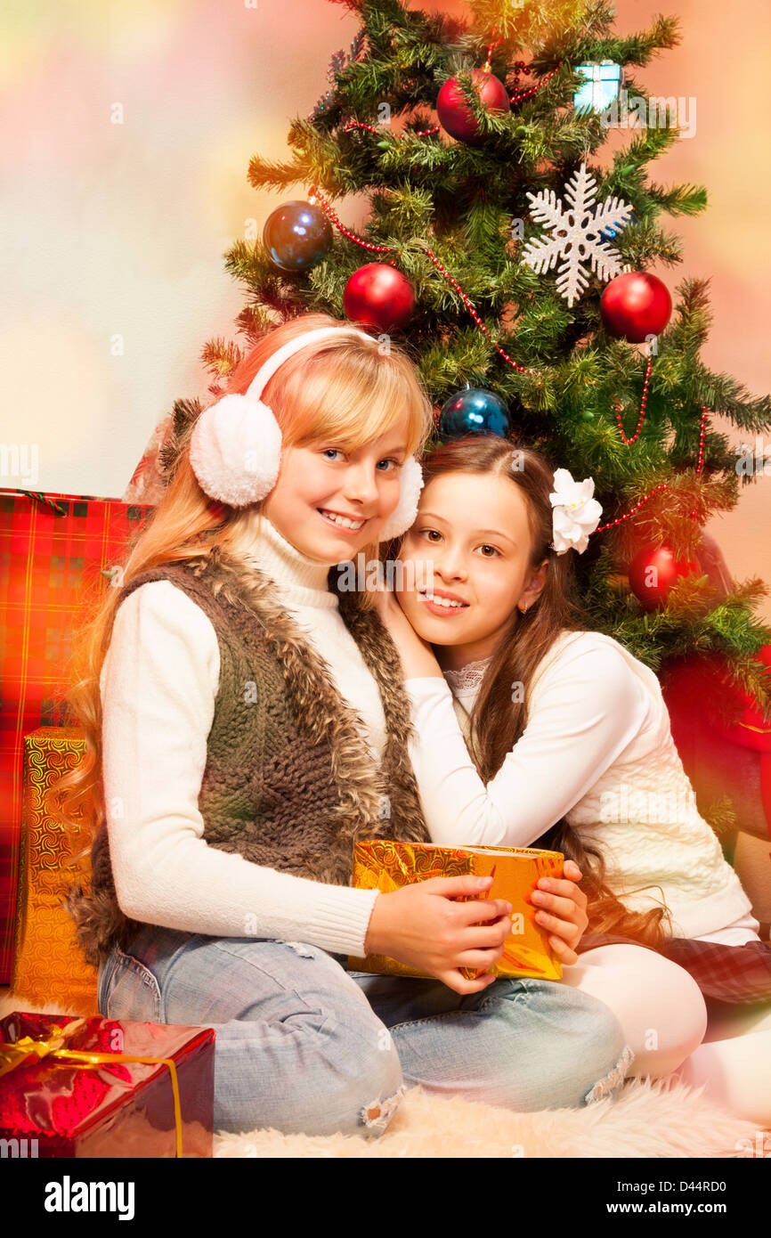 Two sisters sitting near Christmas tree with presents Stock Photo - Alamy
