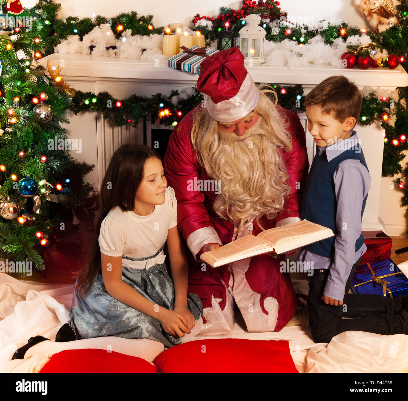 Santa reading Christmas book to kids sitting by decorated tree with boy ...