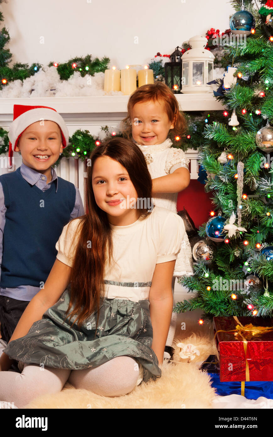 Three kids sitting under Christmas tree and smiling waiting to open ...