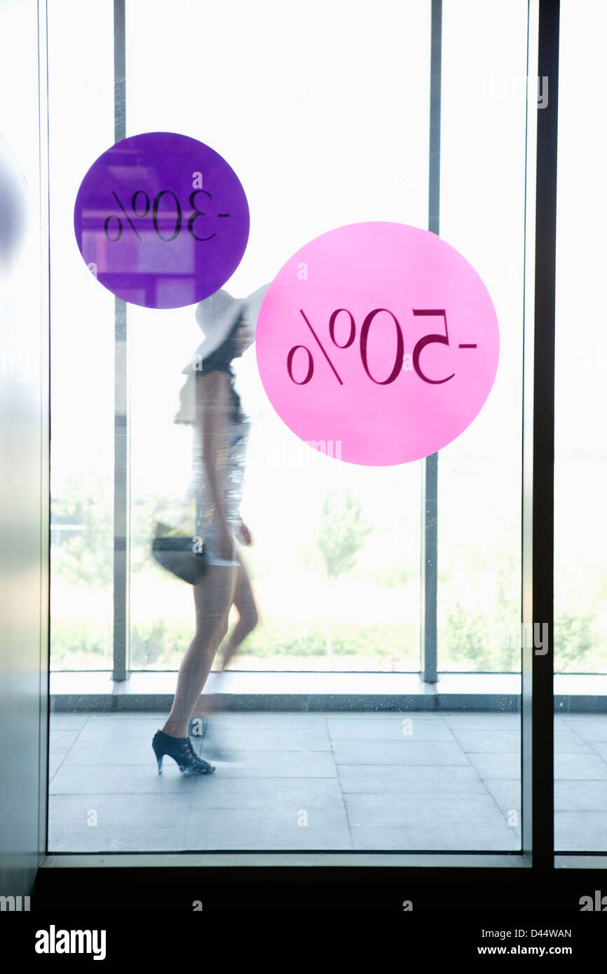 a woman walking along a shopping window with sale sign Stock Photo - Alamy