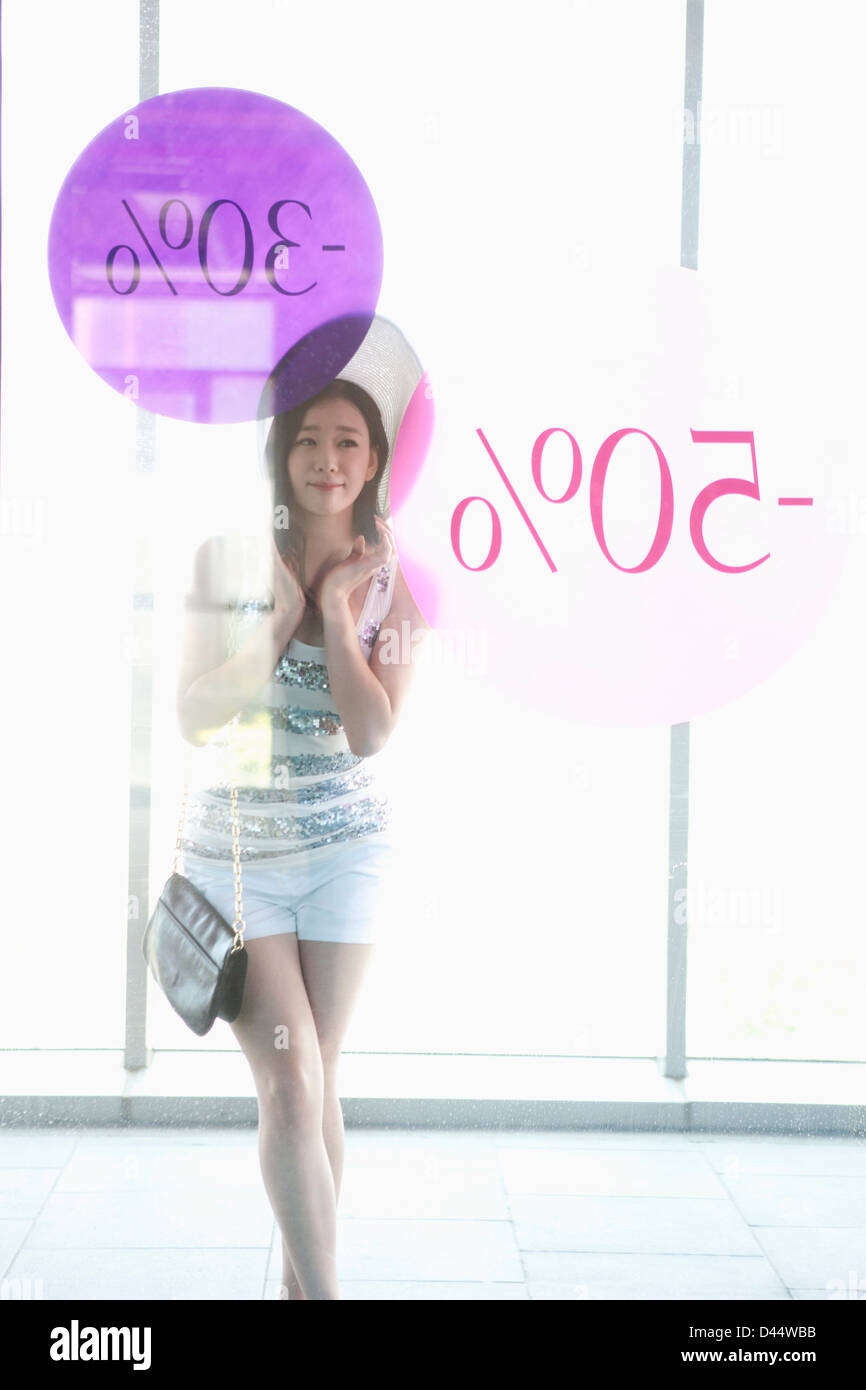 a woman looking through a shopping window with sale sign Stock Photo ...