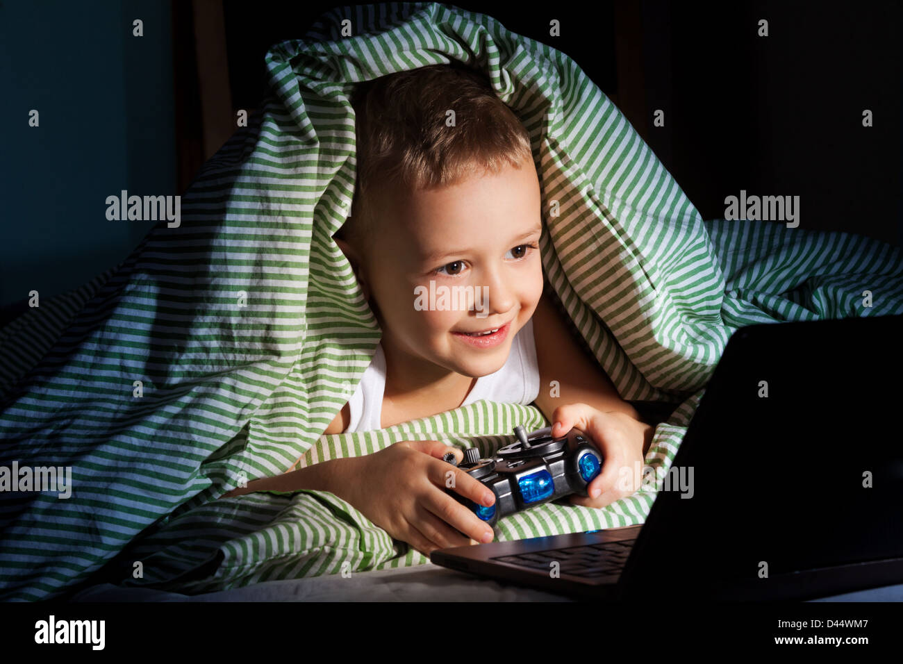 five years old happy kid hiding under blanket playing computer games ...