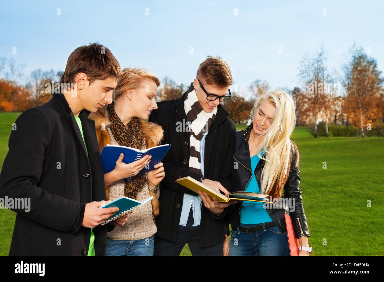 Four students discussing subject in the park standing with books and ...