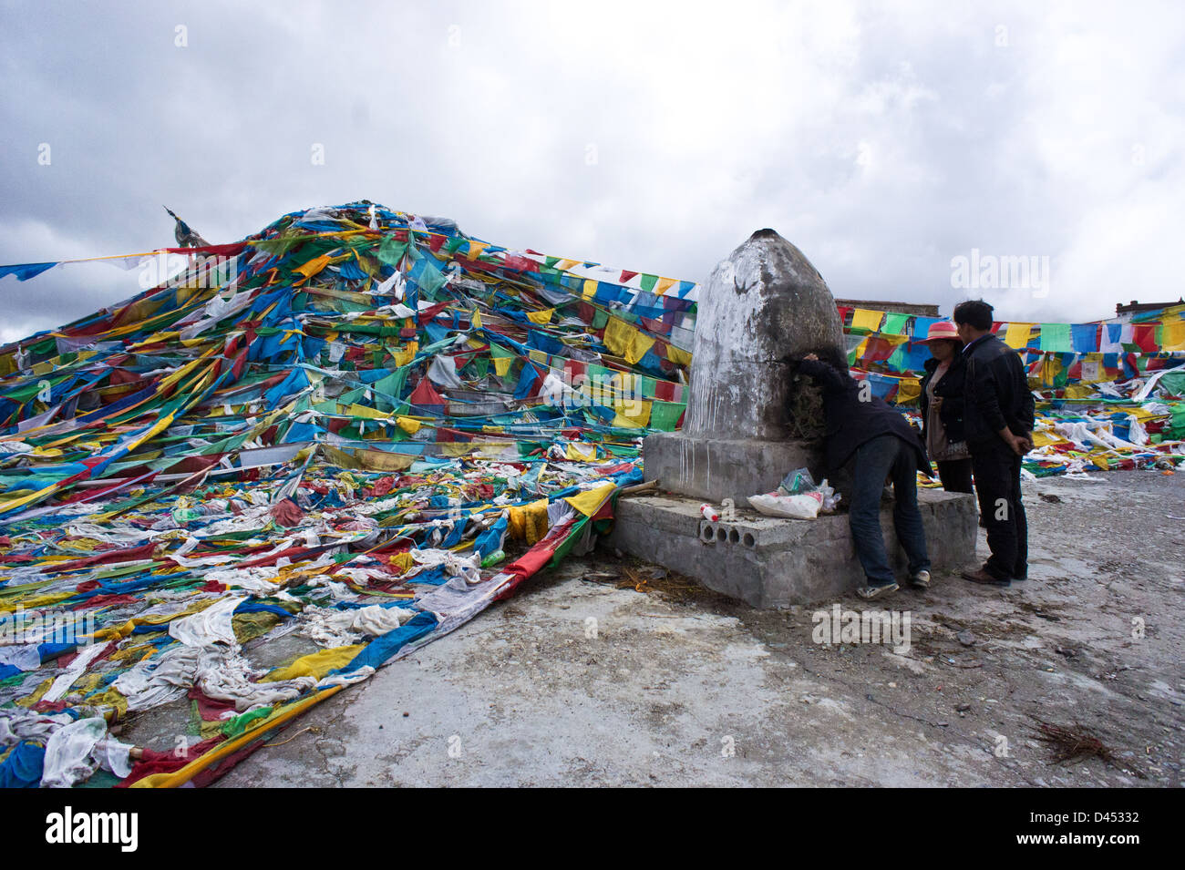 Tibetan burning Juniper branches in front of pile of prayer flags ...