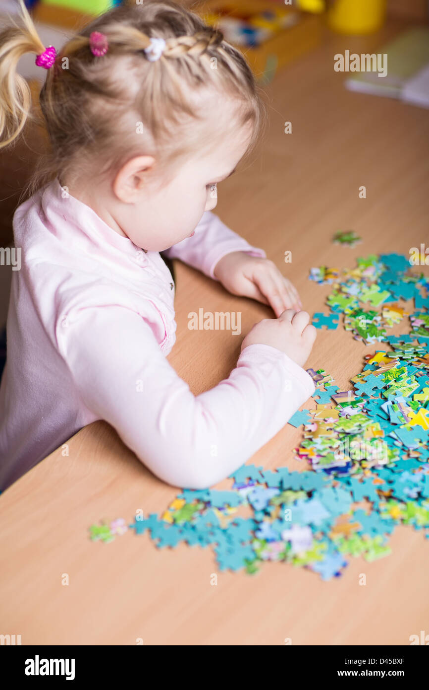 Cute little girl playing puzzles at the table Stock Photo - Alamy