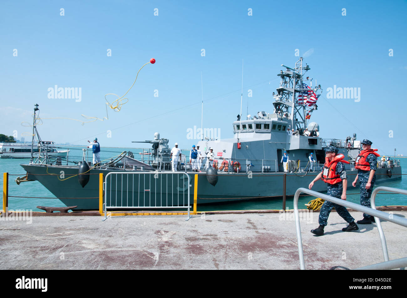 A sailor throws a heaving line aboard a ship to facilitate ...