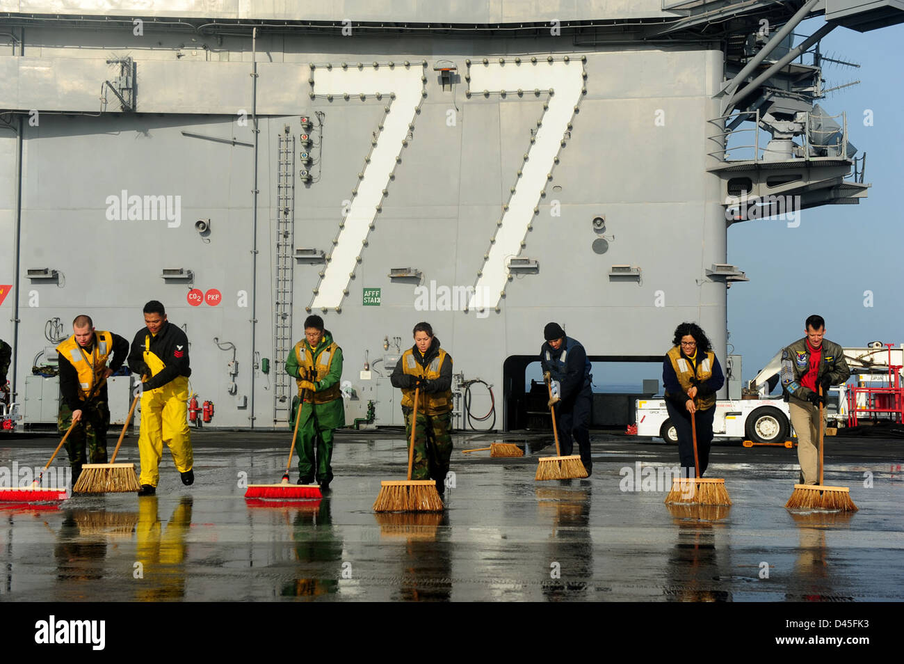 Sailors aboard a U.S. Navy ship scrub the flight deck to maintain ...
