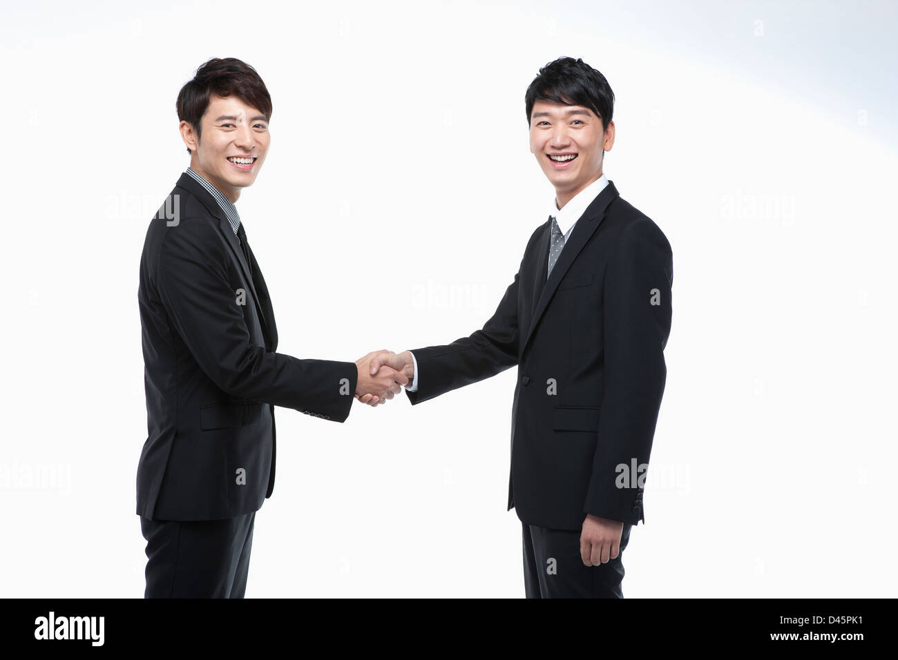 two young businessmen looking at camera while shaking hands Stock Photo ...