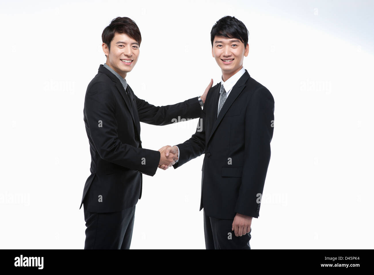 two young businessmen looking at camera while shaking hands Stock Photo ...