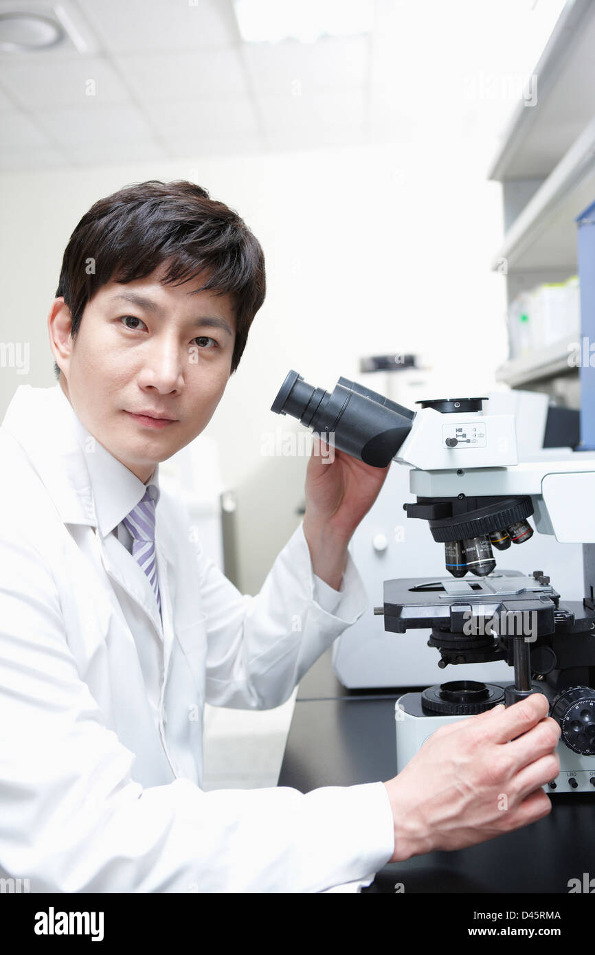 a doctor posing at camera while looking through microscope Stock Photo ...