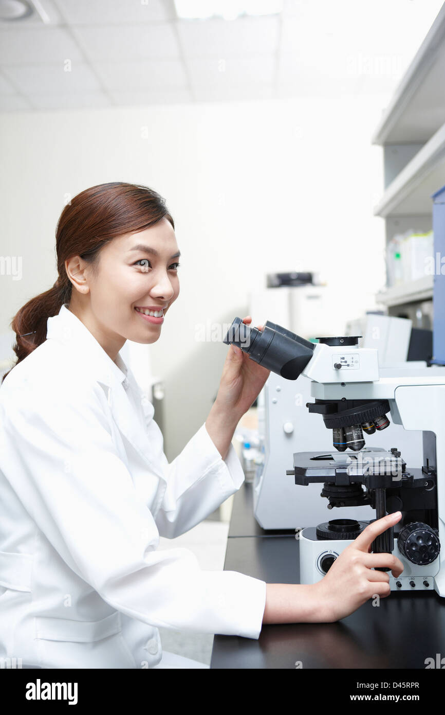 a female doctor smiling while looking through a microscope Stock Photo ...
