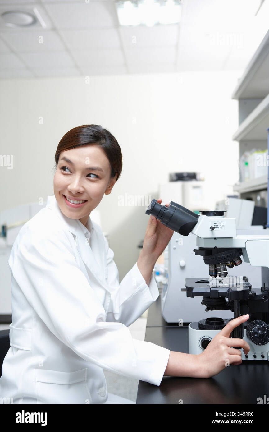 a female doctor smiling while looking through a microscope Stock Photo ...