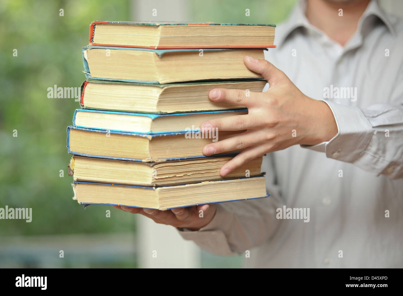 Guy in a shirt holding a stack of old books Stock Photo - Alamy