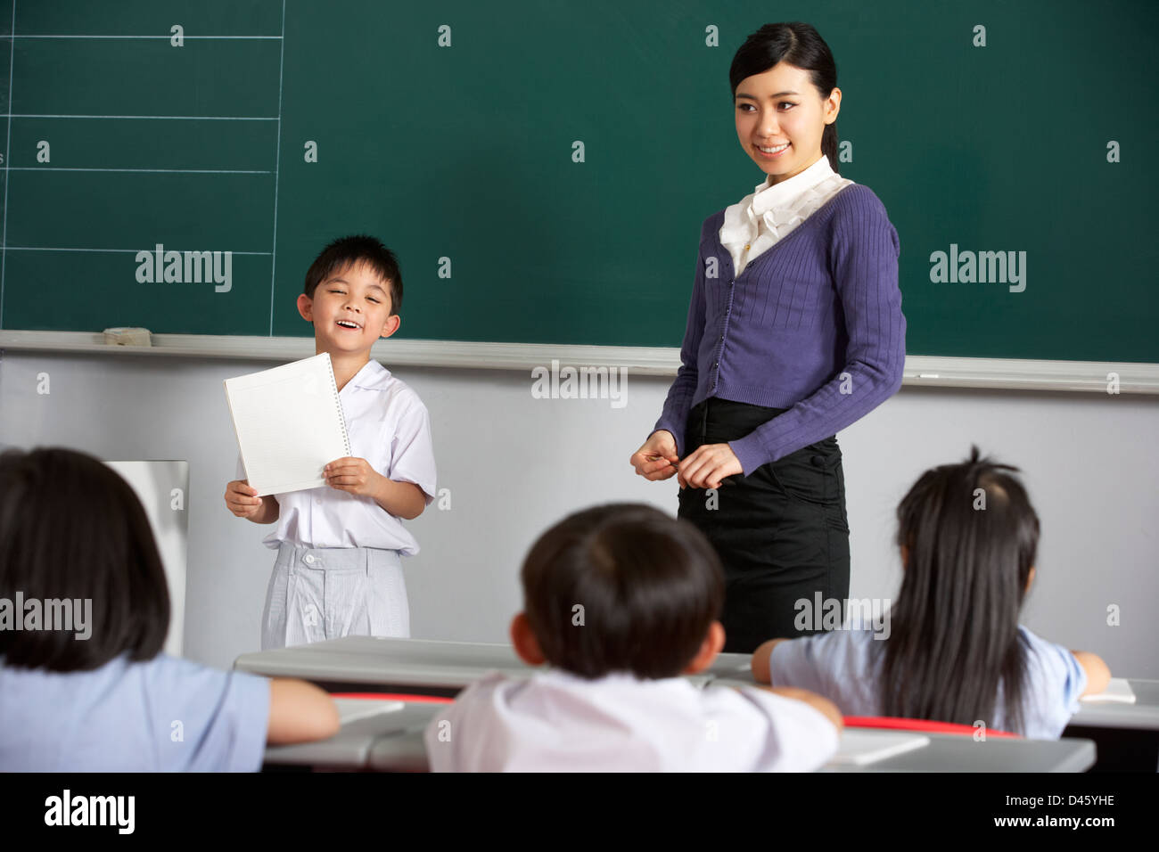 Pupil And Teacher Standing By Blackboard In Chinese School Classroom ...