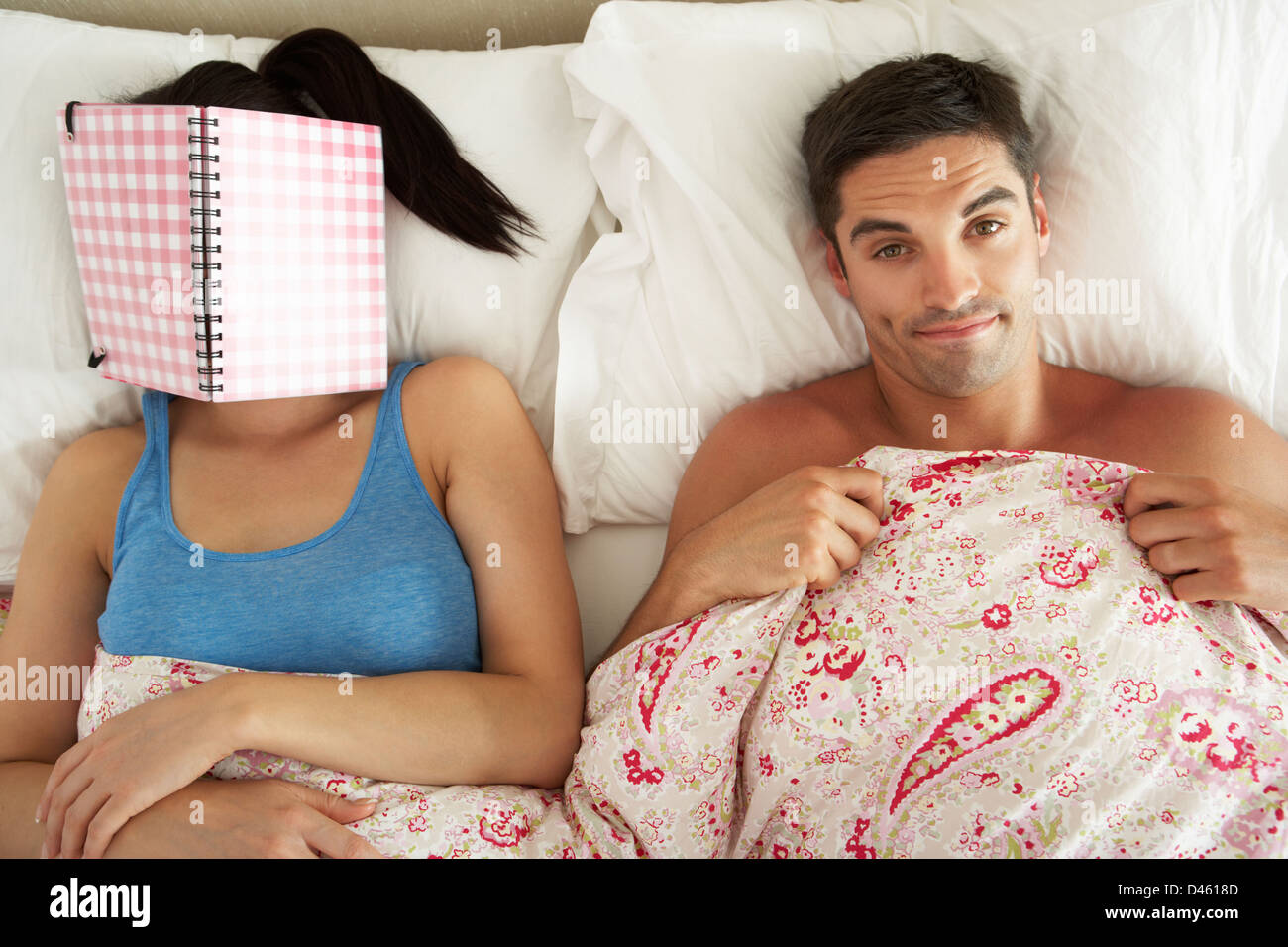 Bored Looking Man Lying In Bed Next To Woman Reading Book Stock Photo ...