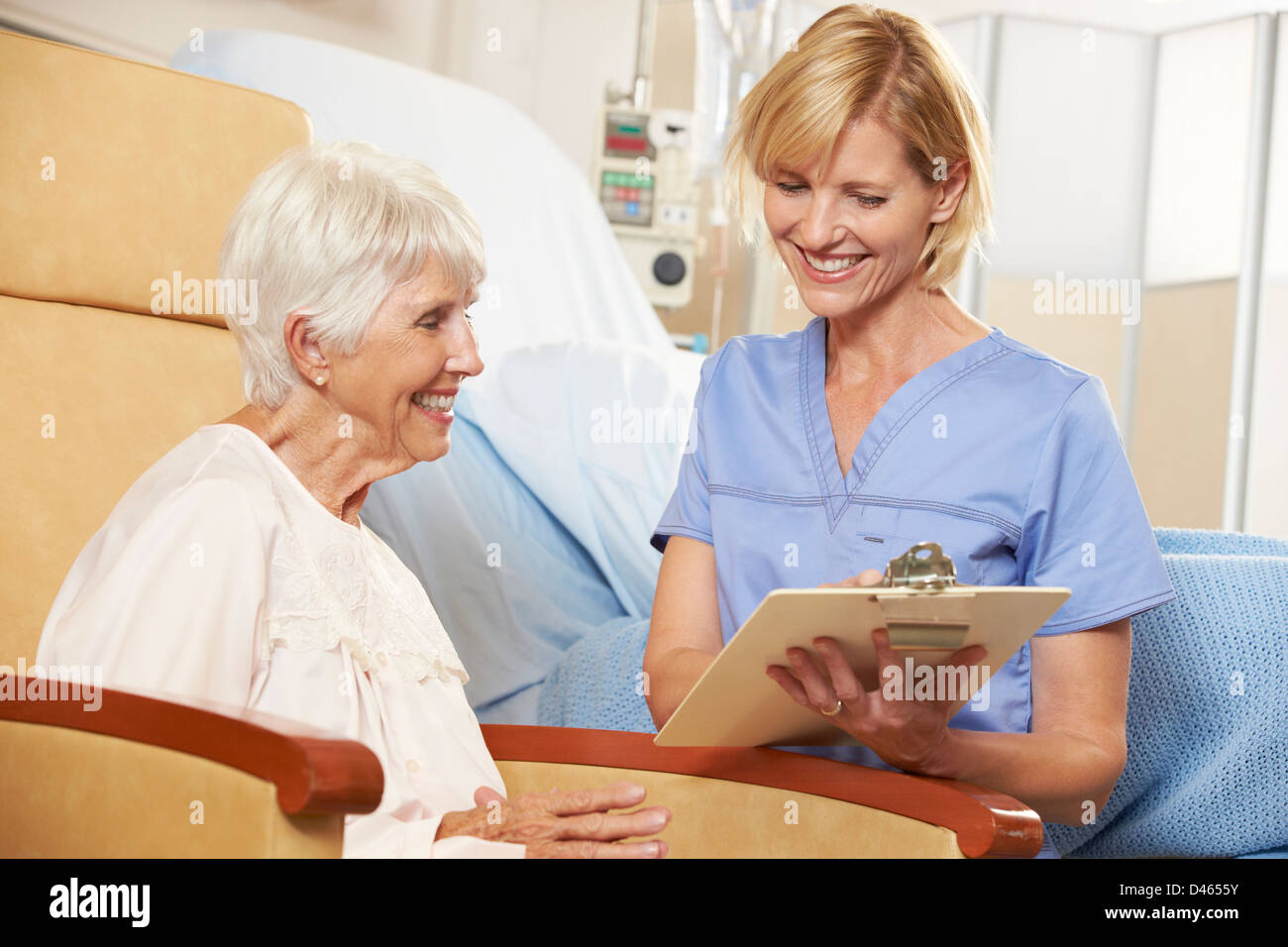 Nurse Taking Notes From Senior Female Patient Seated In Chair By ...