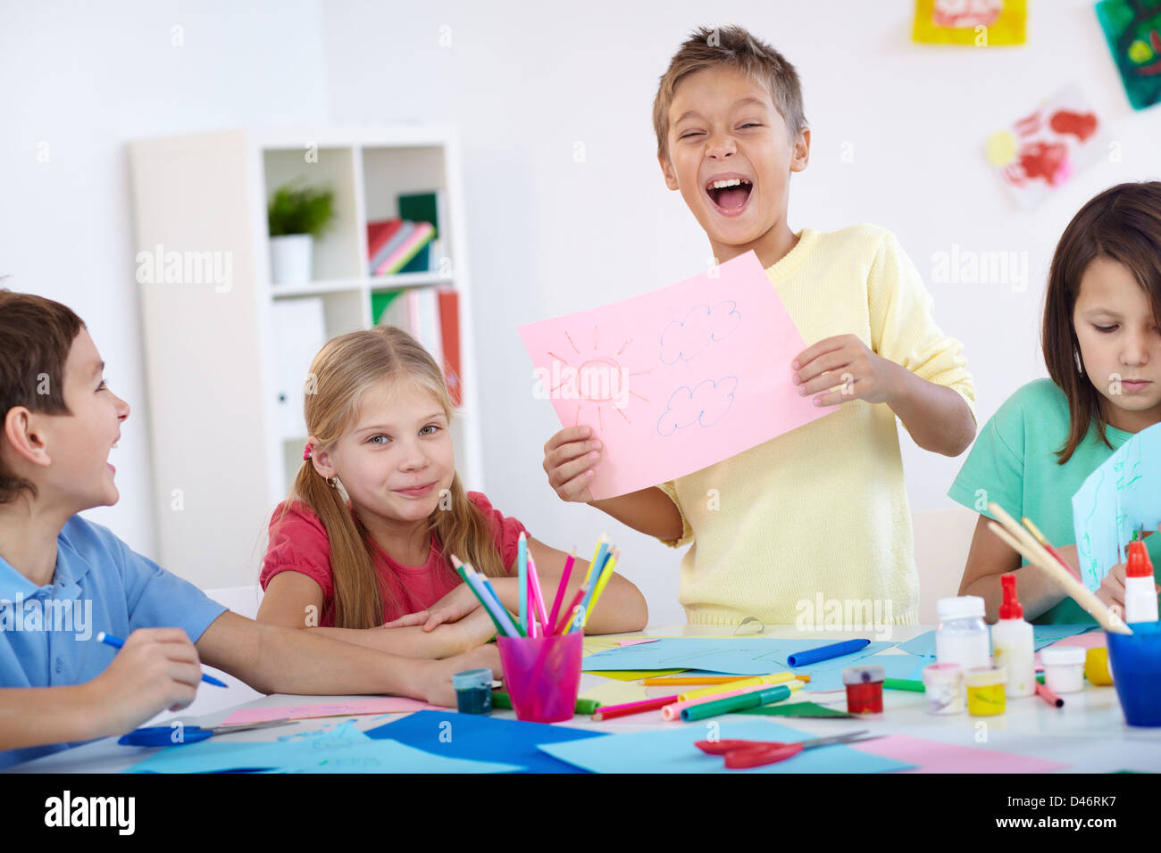 Glad little boy showing his drawing to his friends in classroom Stock ...