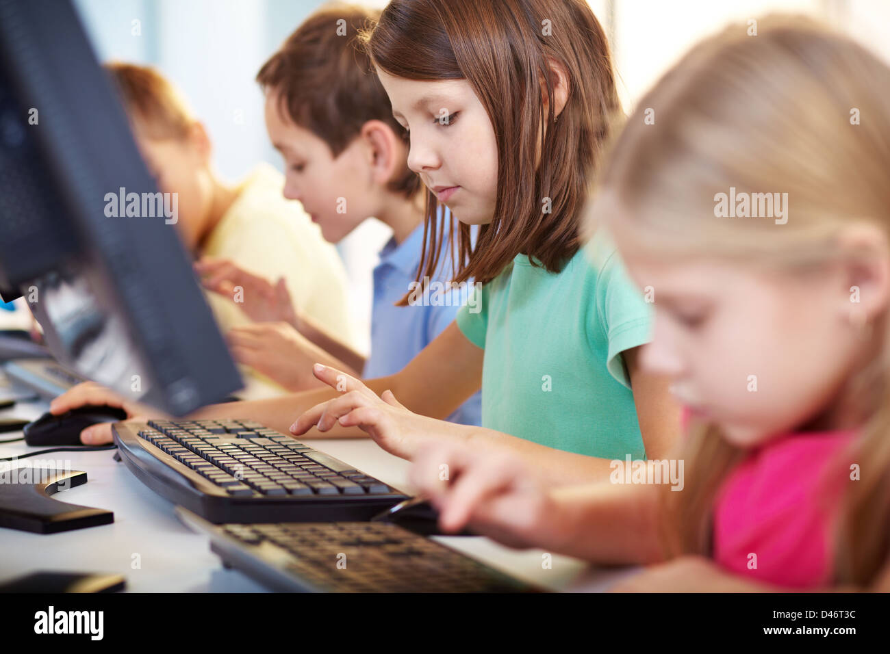 Portrait of lovely schoolgirl looking at computer keyboard while typing ...