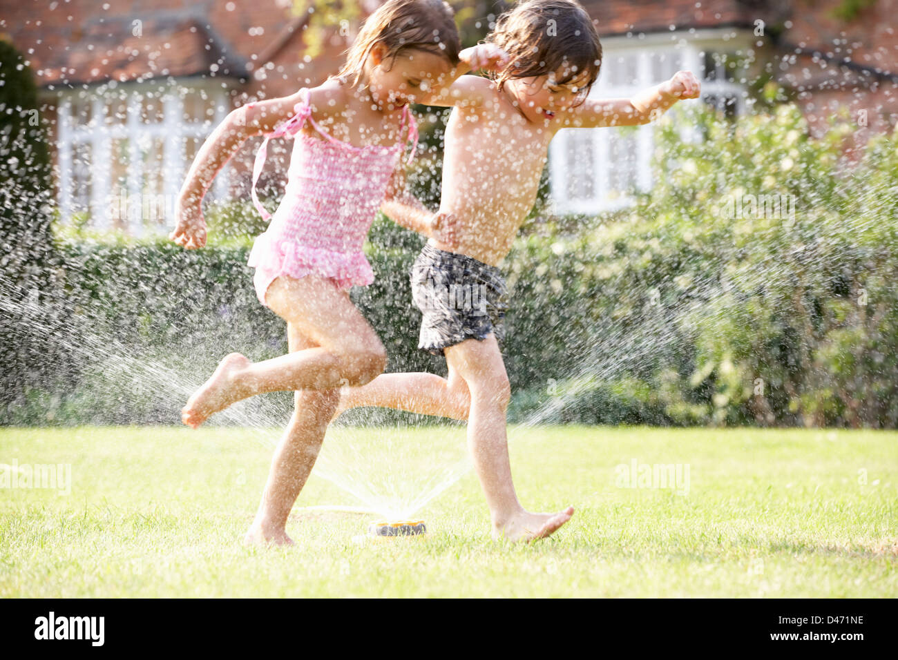 Two Children Running Through Garden Sprinkler Stock Photo - Alamy
