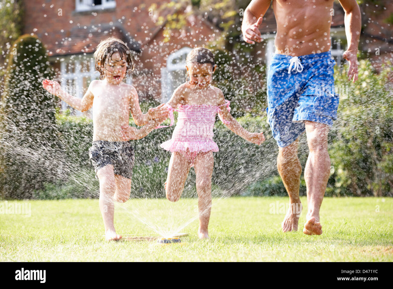 Father And Two Children Running Through Garden Sprinkler Stock Photo ...