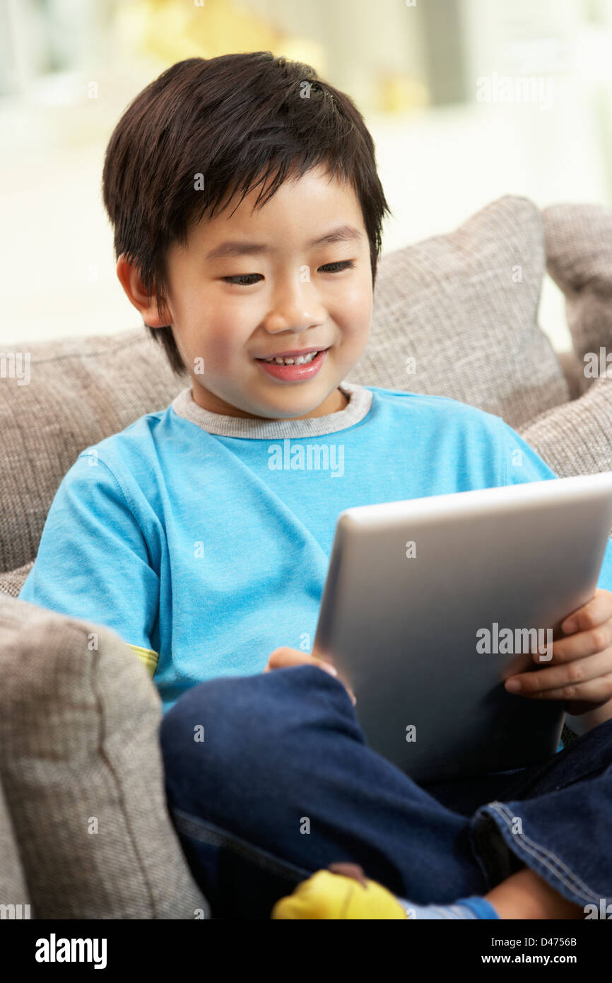 Young Chinese Boy Using Tablet Computer Whilst Sitting On Sofa At Home ...