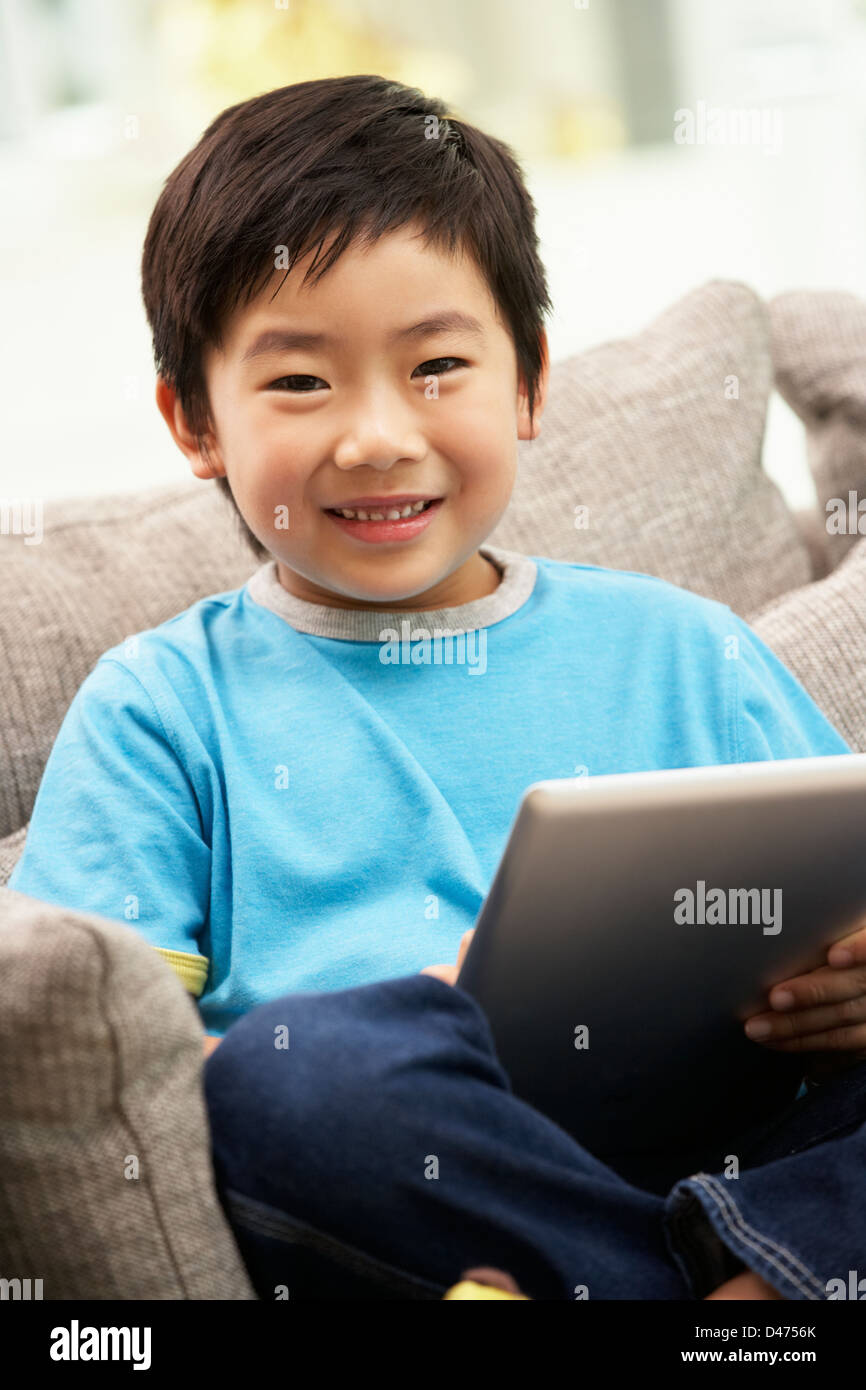 Young Chinese Boy Using Tablet Computer Whilst Sitting On Sofa At Home ...