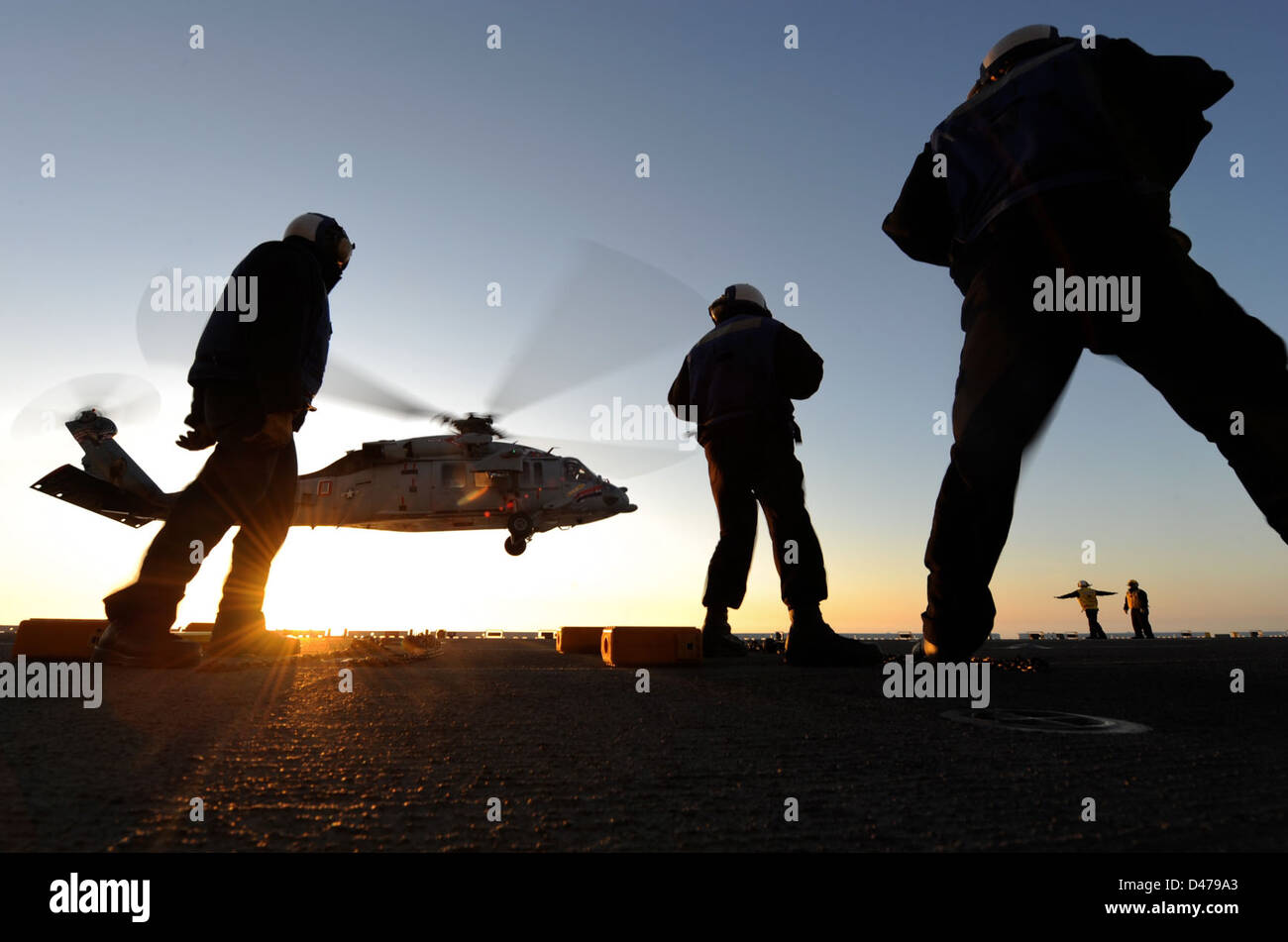 Sailors maintain position as a helicopter lifts off from the deck of a ...