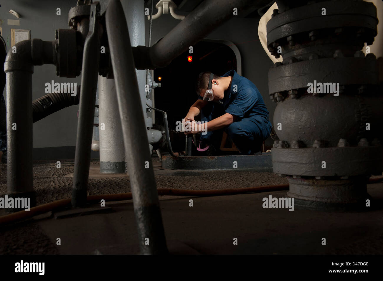 A U.S. Navy Sailor chips paint on the hull of a ship as part of ...
