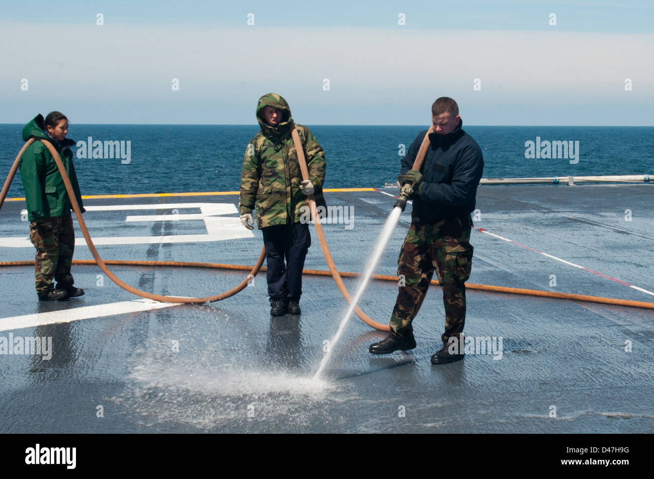 Sailors aboard a U.S. Navy vessel hose down the flight deck following a ...