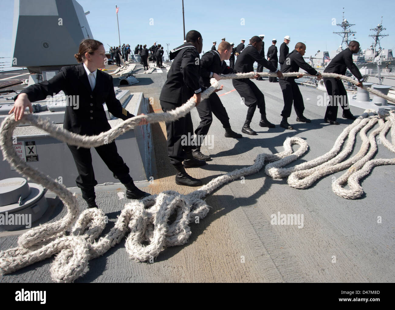 Sailors aboard a ship heave in a line, preparing for deployment, as ...