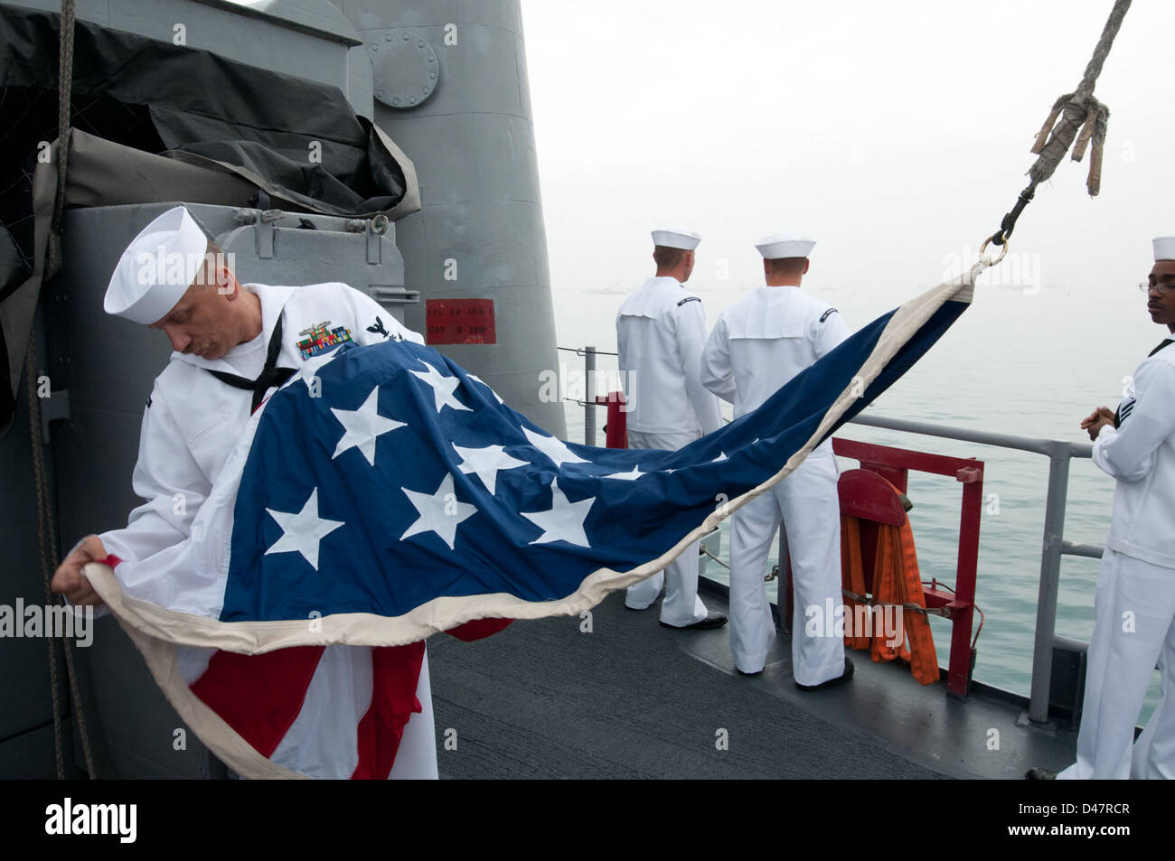 Sailors aboard a U.S. Navy ship raise the ensign during a ceremony in ...