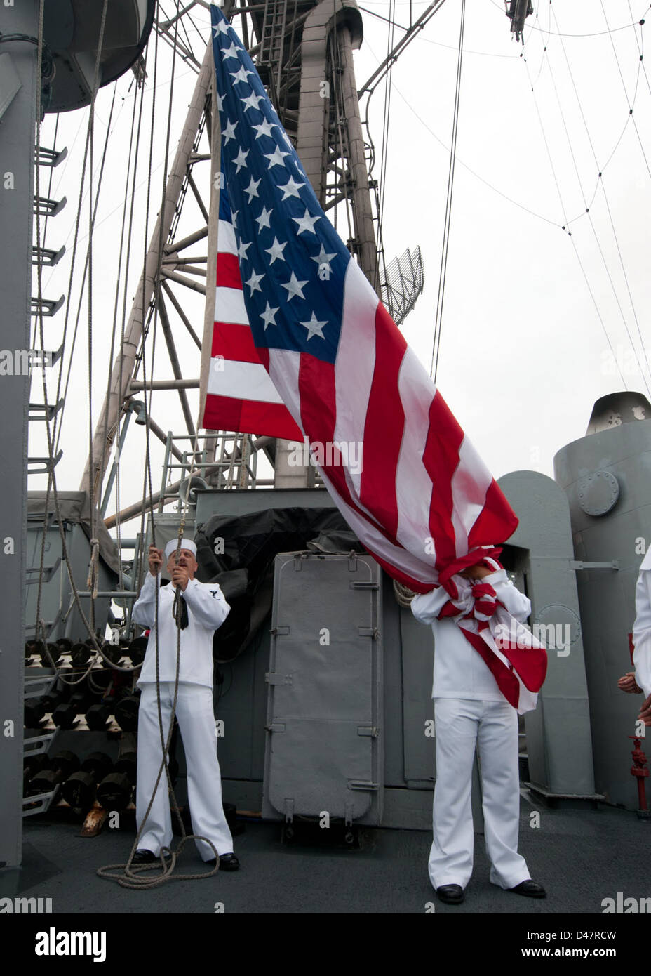Sailors aboard a U.S. Navy ship raise the American ensign during a port ...