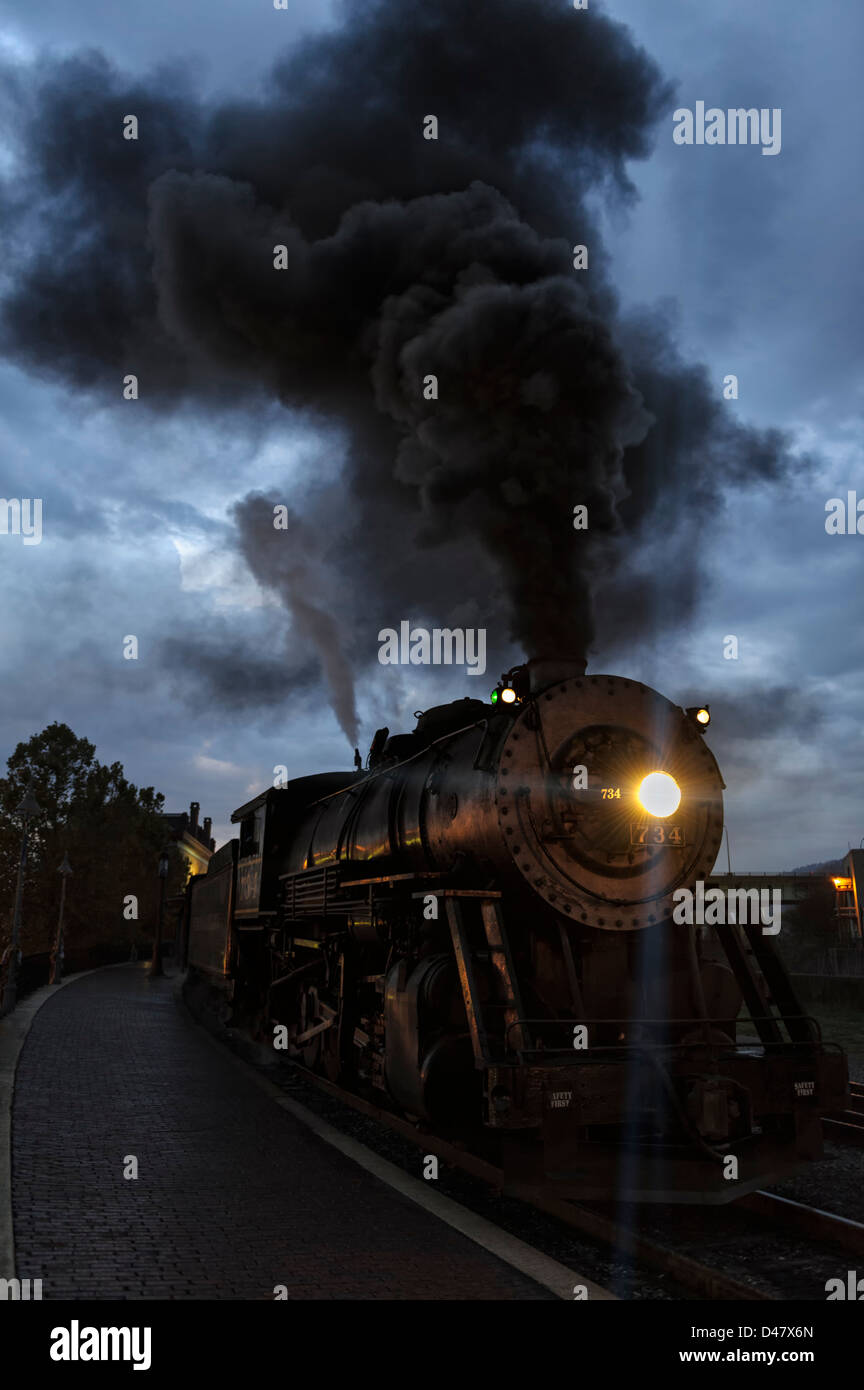 Steam locomotive with train at dawn making black smoke, waiting at the ...
