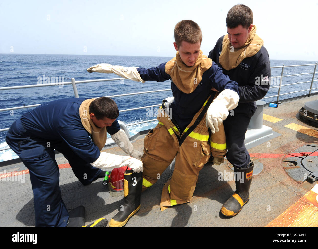 A Sailor receives assistance with donning a firefighting suit during a ...