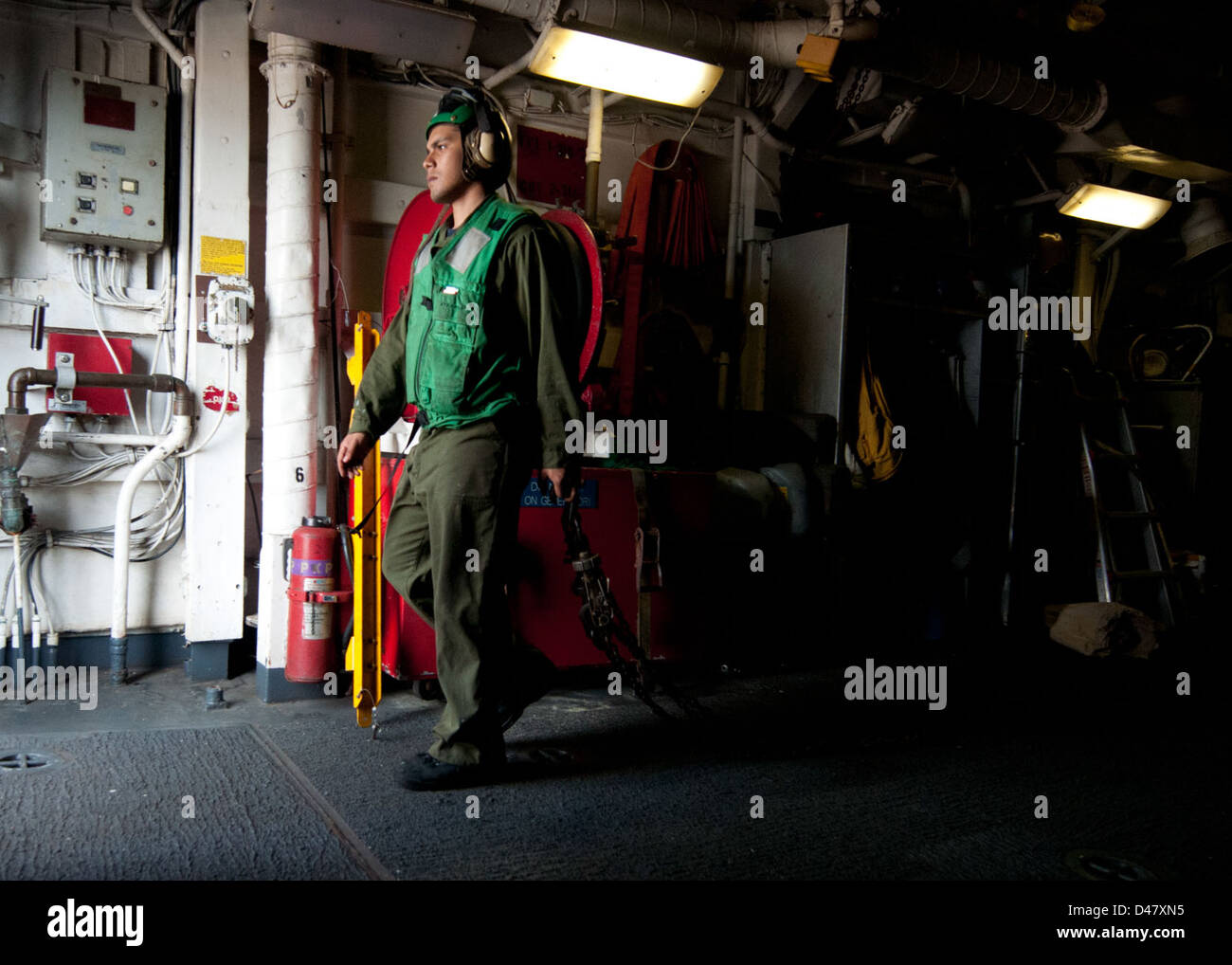A Sailor drags chains across the flight deck of a naval vessel ...