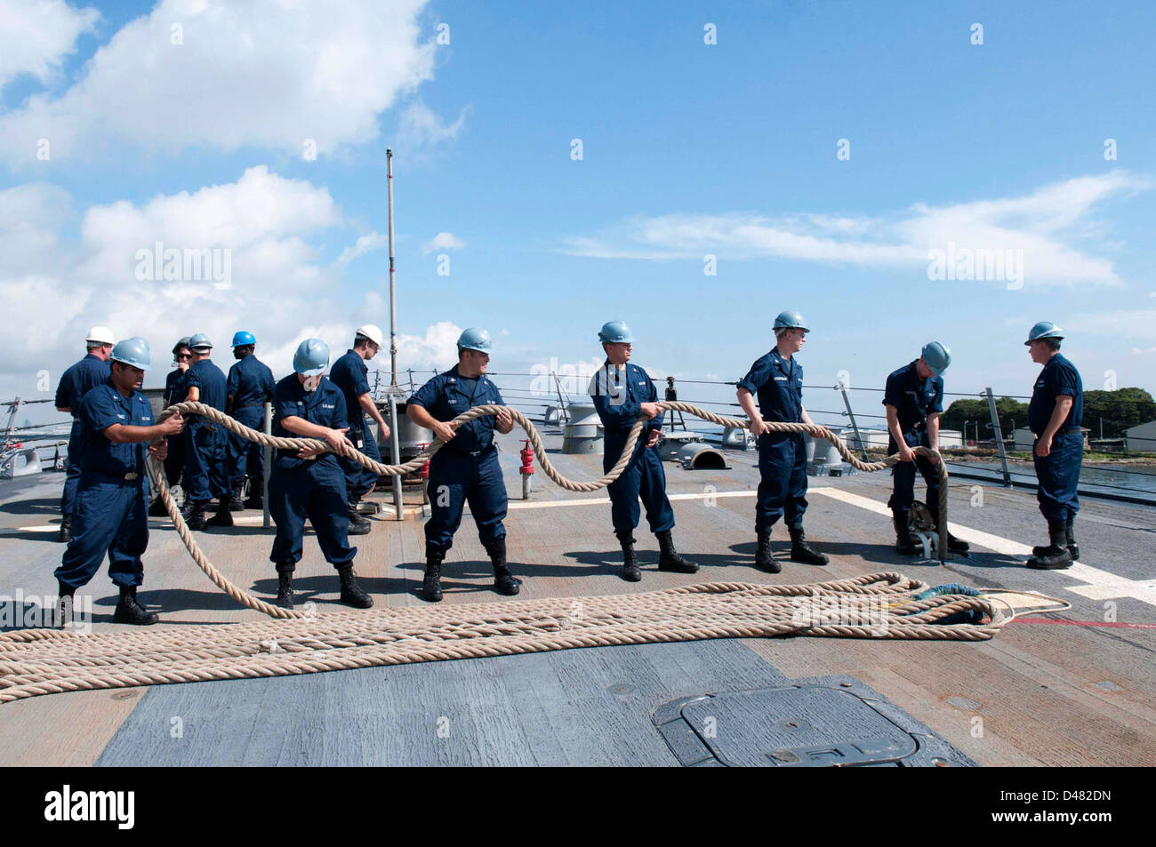 Sailors aboard the USS Mustin move the ship's lines into storage ...