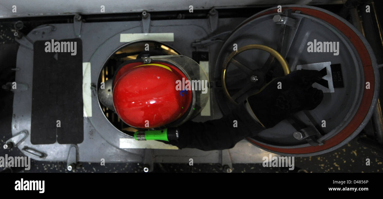 A U.S. Navy Sailor climbs down an escape scuttle on a ship, performing ...