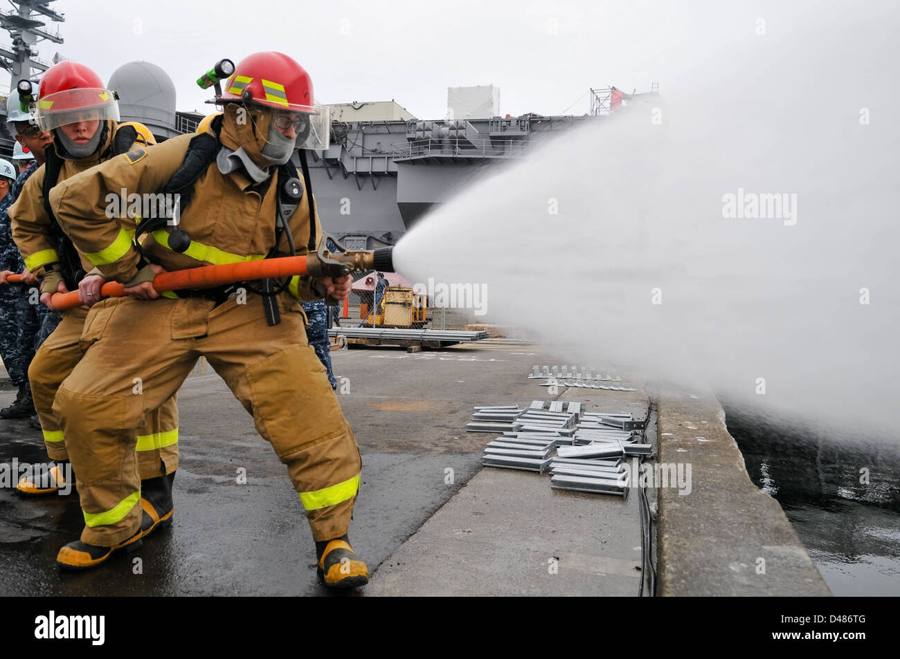 Sailors aboard a U.S. Navy vessel practice using a live fire hose ...