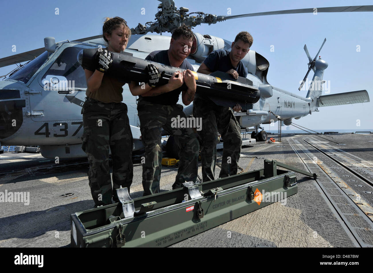 Sailors aboard a U.S. Navy SH-60B helicopter load a Hellfire missile, preparing the aircraft for ...