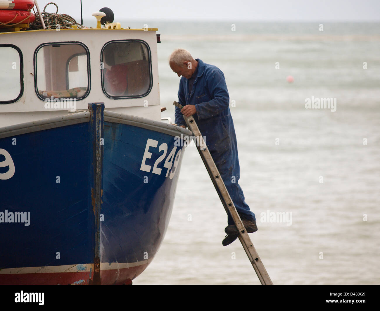 A man does maintenance on fishing boat Stock Photo - Alamy