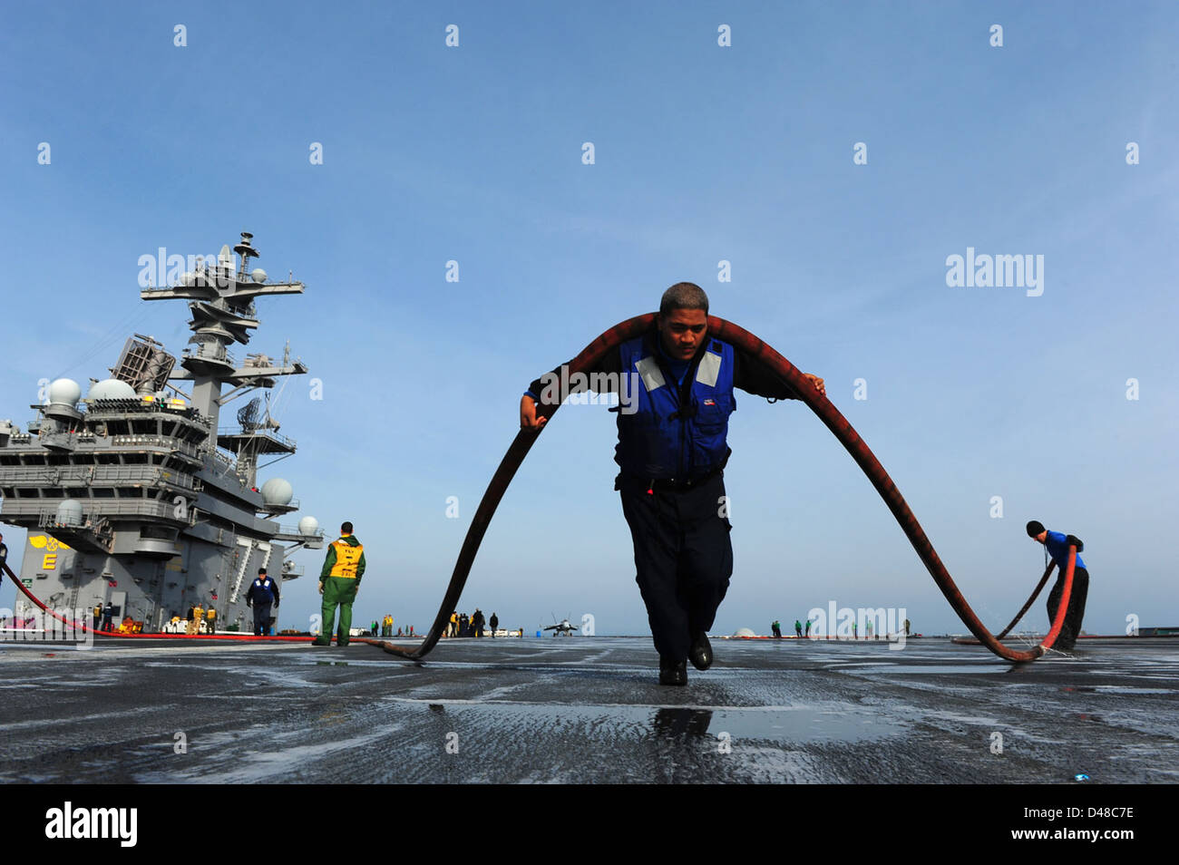 A Sailor aboard a U.S. Navy ship moves a hose as part of daily ...
