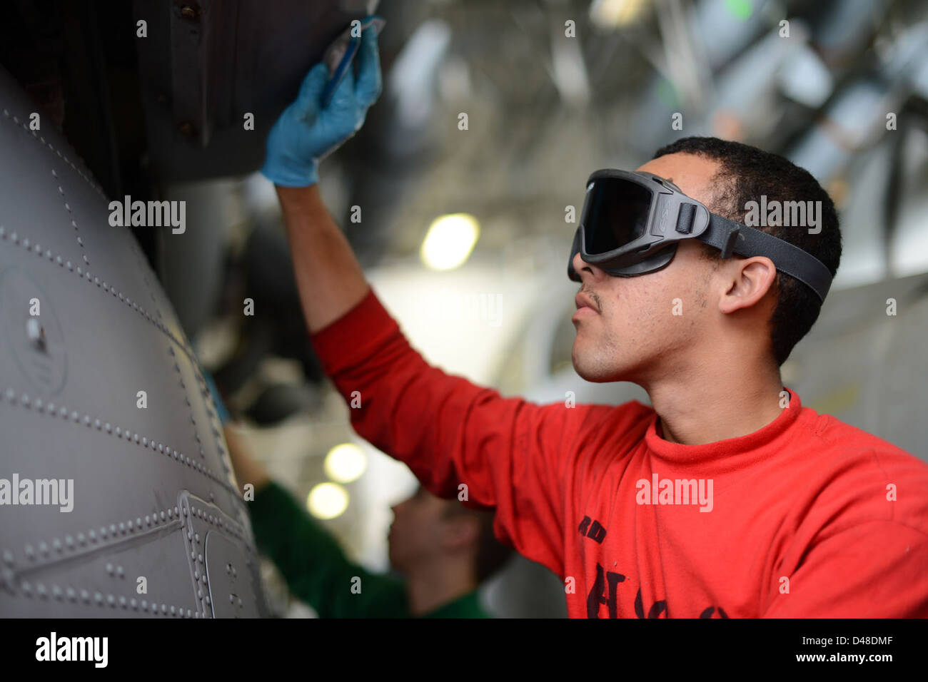 A U.S. Navy sailor services an MH-60S Sea Hawk helicopter, ensuring it ...