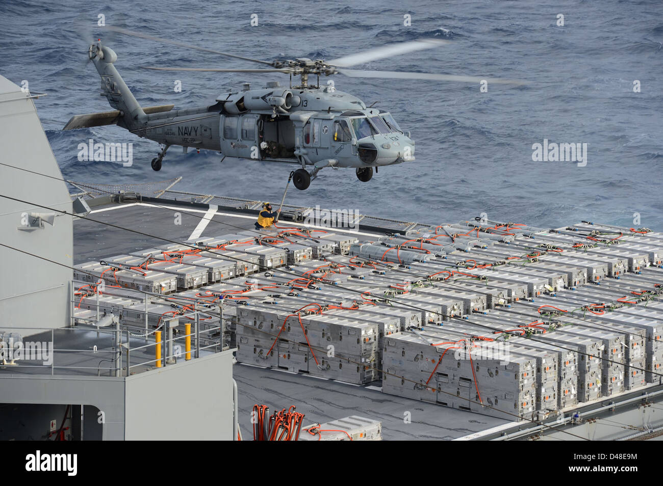An MH-60S helicopter picks up ammunition from a ship at sea, supporting ...