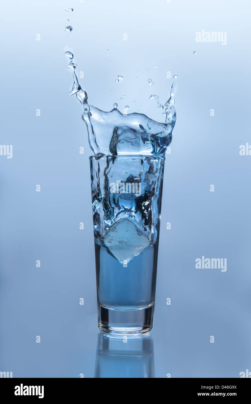 Ice cube falling into glass of water Stock Photo - Alamy