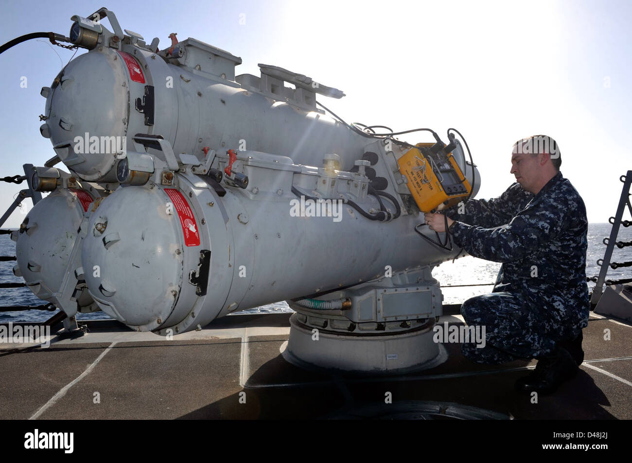 A Sailor performs maintenance on a torpedo tube while deployed at sea ...