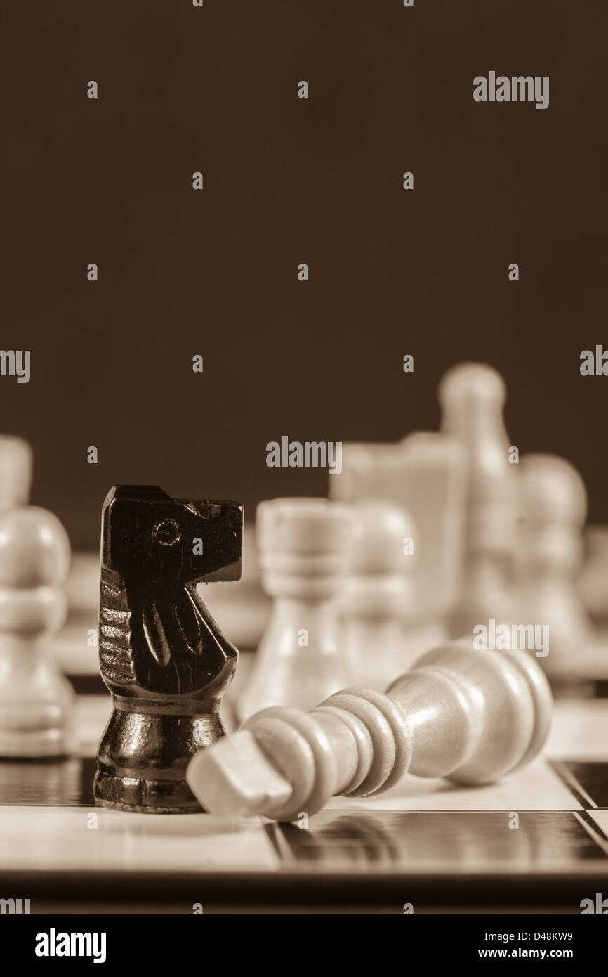 Fallen white chess piece lying next to black knight in sepia tone Stock ...