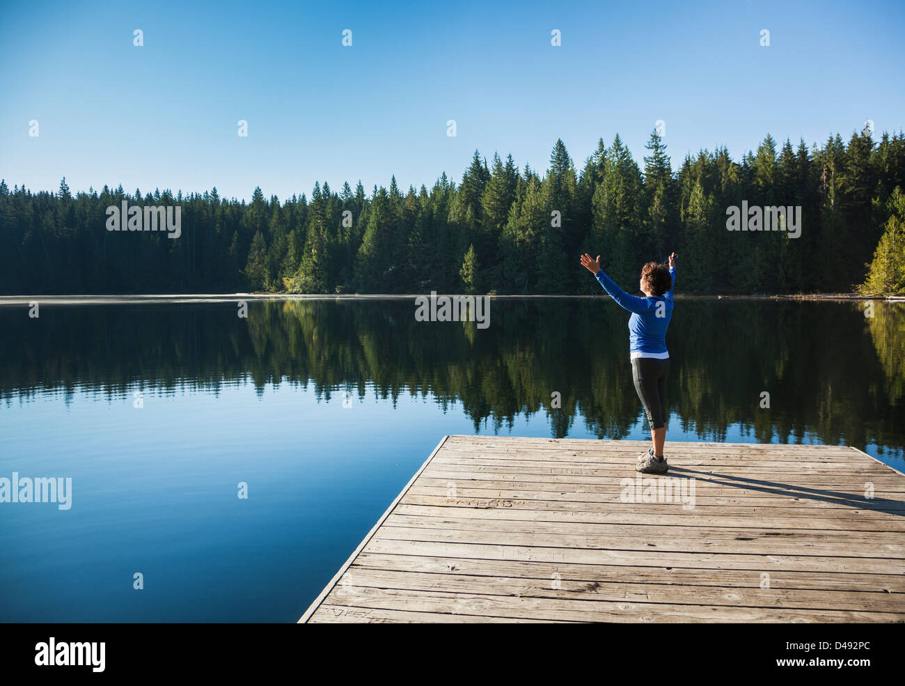 A woman greets the morning sun on a dock on lizard lake;Vancouver ...