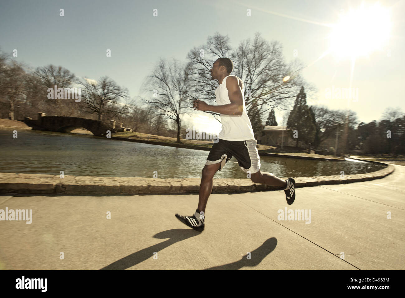 A strong young African American man jogging in a park by a lake Stock ...