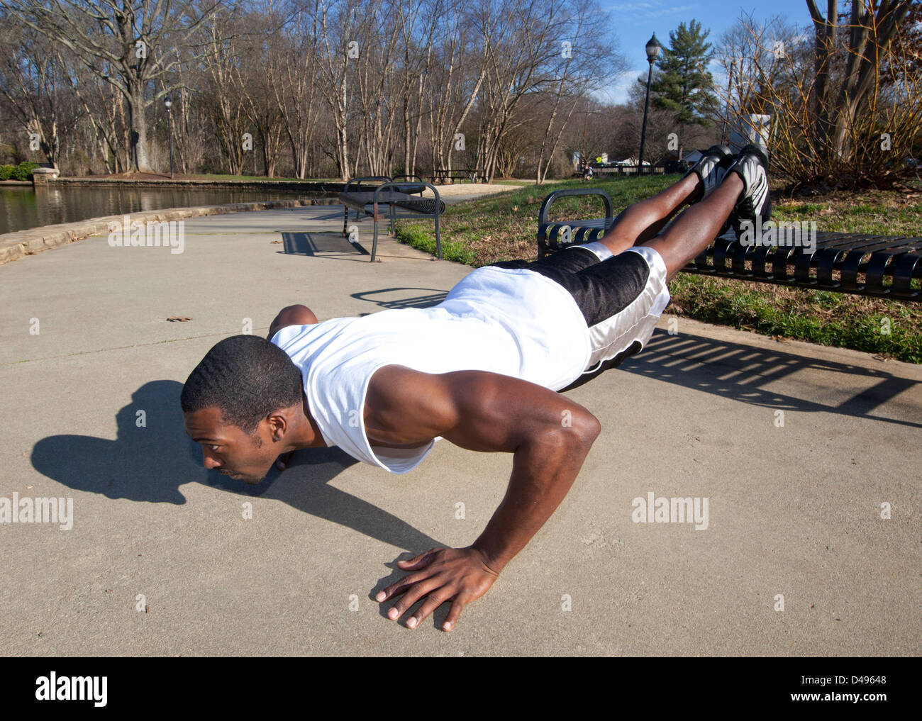 A strong young African American man working out outdoors in a park ...